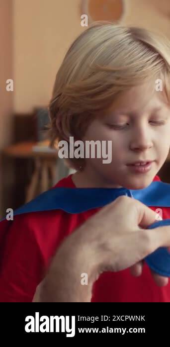 Vertical over shoulder of dad helping tween son to wear blue superhero ...