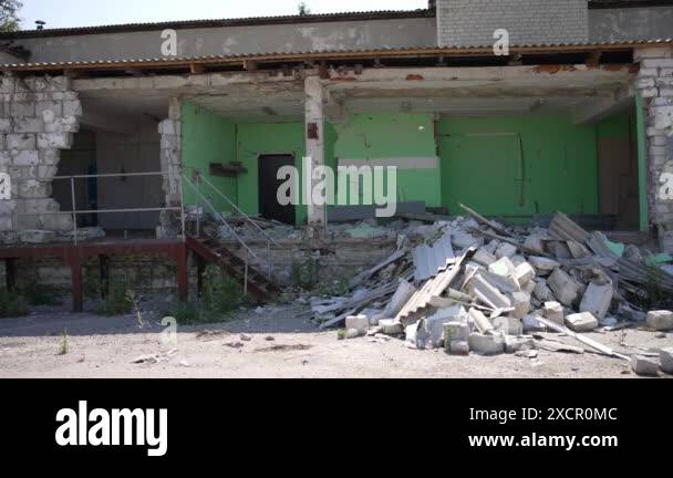 Facade of conflict-damaged farmhouse with debris and missing doors ...