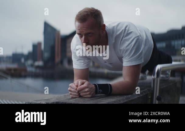 A man performs a plank exercise on a waterfront promenade. The man's ...