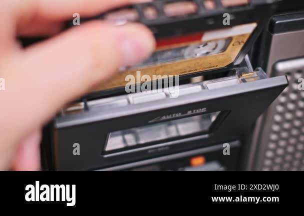 Close-up of a hand inserting an audio cassette into a vintage boombox ...
