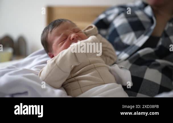 Newborn baby sneezing while resting on mother's lap, capturing a ...