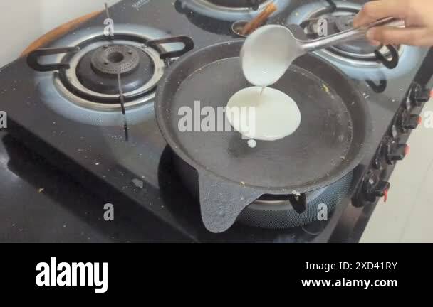 In the kitchen, a woman makes dosa for breakfast by pouring white ...