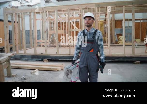 Worker carpenter in uniform walks with tools near unfinished ...