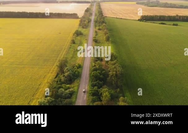 An aerial photograph shows a road running between fields. Green and ...