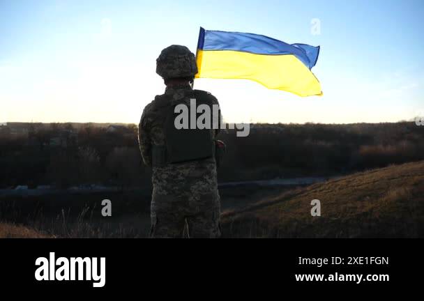 Soldier of ukrainian army stands at hill and holds waving flag of ...