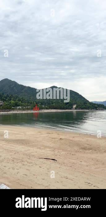 A beach with a red sculpture in the water. The great Torii of the ...