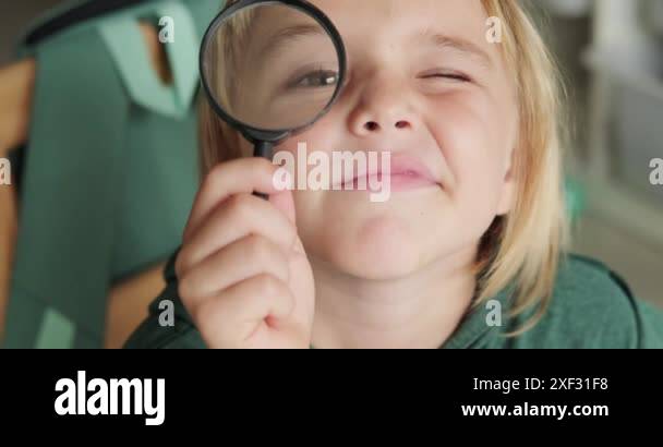 Portrait of a boy from elementary school who holds a magnifying glass ...