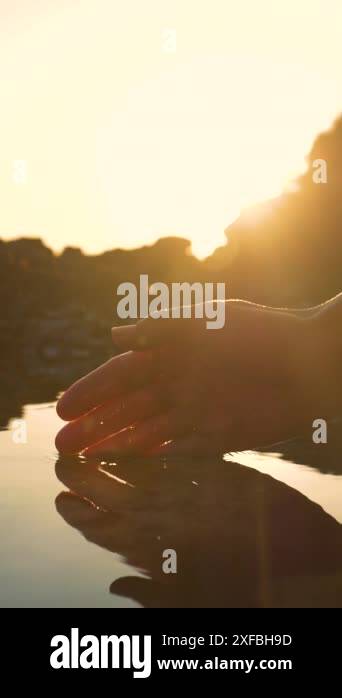 LENS FLARE, VERTICAL, DOF: Sunshine and a hand scooping water from sea ...