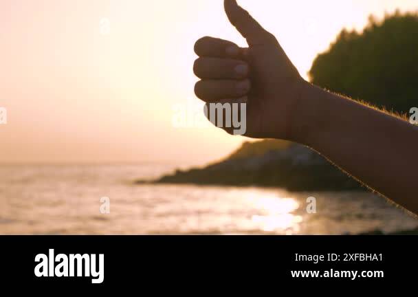 LENS FLARE, SILHOUETTE: A thumbs up against the tranquil sunset by the ...