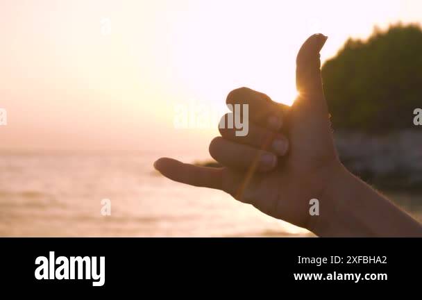 LENS FLARE, CLOSE UP, SILHOUETTE: Shaka hand gesture against golden ...