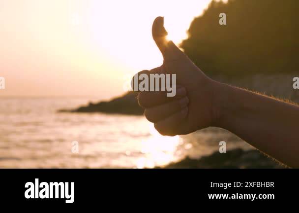 LENS FLARE, CLOSE UP, DOF: Thumbs up to a seascape bathing in golden ...