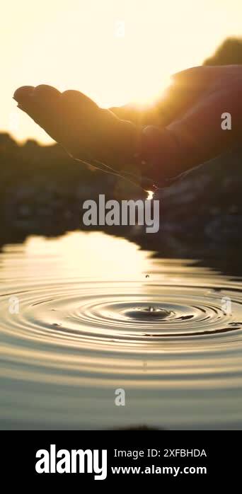 LENS FLARE, VERTICAL: Falling drops from hand scooped water glisten in ...