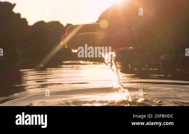 CLOSE UP, LENS FLARE: Sunbeams peep through a hand scooping water in ...