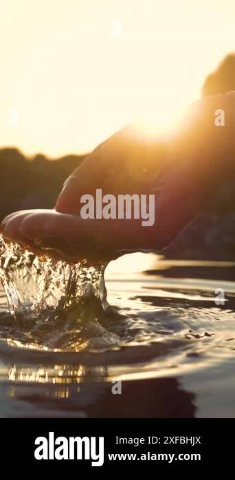 LENS FLARE, VERTICAL, CLOSE UP: Hand scoops water at beach puddle and ...