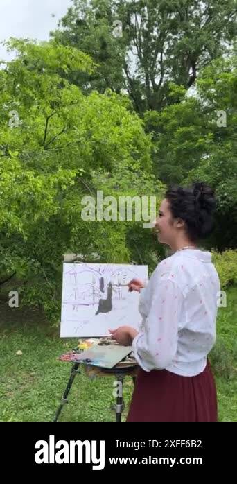Young female artist paints picture in summer park in sunlight. Art and ...