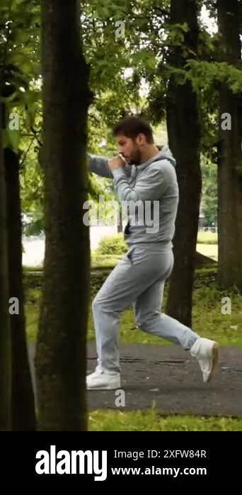 Young powerful Runner boxer in green park on asphalt road waving his ...