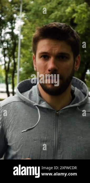 Young attractive powerful sport man run in the park in gray jacket. He ...