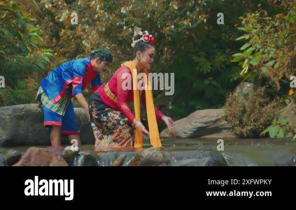 Two people in traditional attire performing a ritual in a river ...