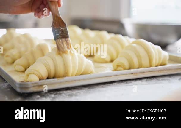 Prepare croissant for bake in oven. Female baker smears raw croissants ...