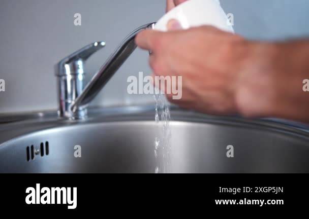 Faucet and water jet pouring, hands washing white mug. Detailed view of ...