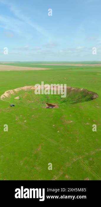 The drone flies over a huge crater from a nuclear explosion in a field ...