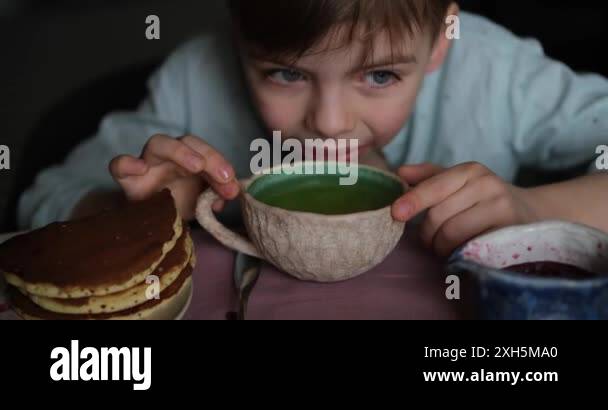Little adorable boy drinking tea for breakfast with pancakes and apples ...