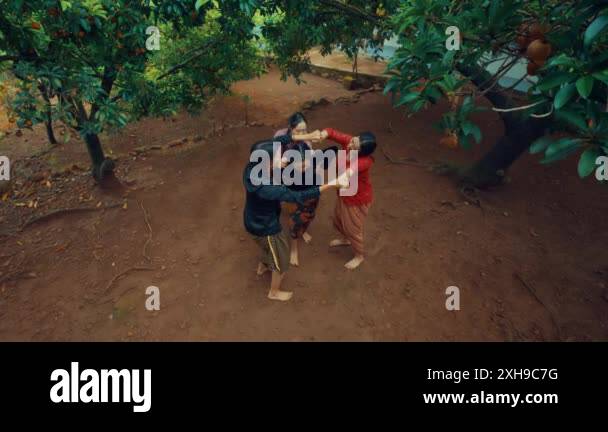 A group of people playing a traditional game outdoors under fruit trees ...