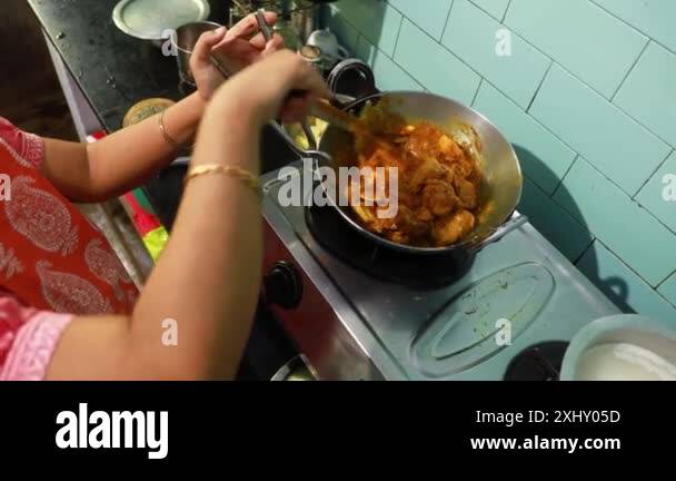 An Indian housewife wearing cooking apron in kitchen making chicken ...