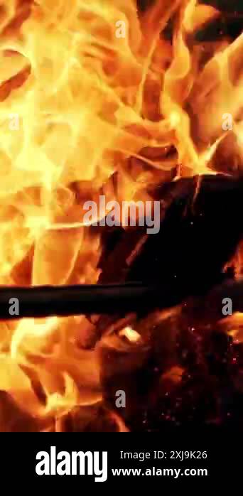 Wooden stick is mixing logs in bright fire. Orange flame from burning ...