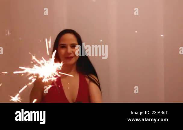 Long-haired Caucasian woman in a cocktail dress watches the firework sparkler light as she ...