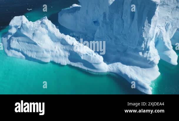 Close up aerial iceberg calving blue ocean water. Huge high snow covered ice formation floats ...