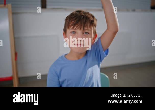 Small boy raising hand at lesson closeup. Smiling pupil listening ...