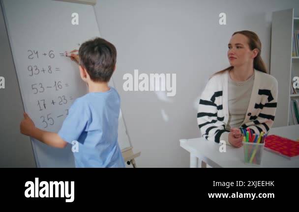 Clever schoolboy writing task on whiteboard closeup. Female tutor ...