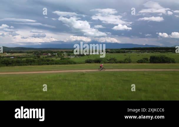 Drone following woman cyclist riding bike in incredible epic landscape surrounded by mountains ...