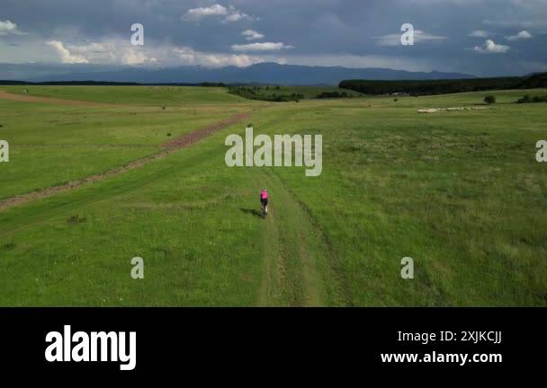 Drone following woman cyclist riding bike in incredible epic landscape surrounded by mountains ...