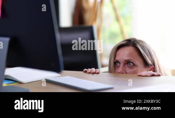 Scared woman peeks out from under table looking at screen of computer ...