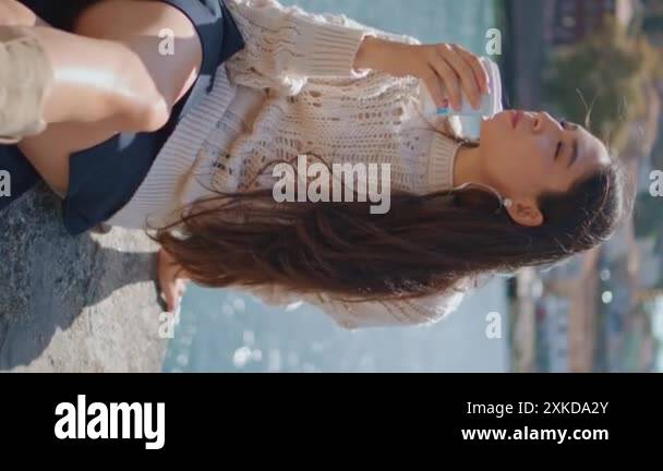Relaxed model holding takeaway drink resting at sunny river embankment ...