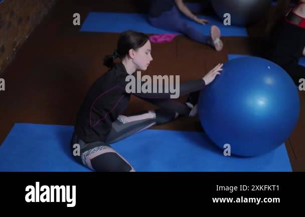 Women in sportswear, sitting on fitness mats with legs wide apart, do ...