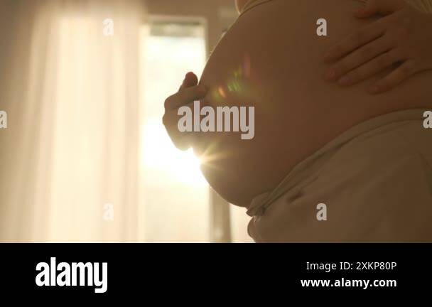 Pregnant woman gently strokes big belly against window. Young female ...