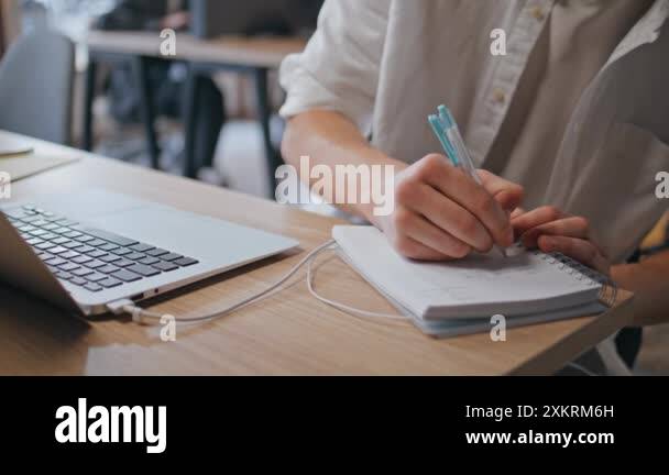 Office worker hands noting information in notebook working at laptop ...