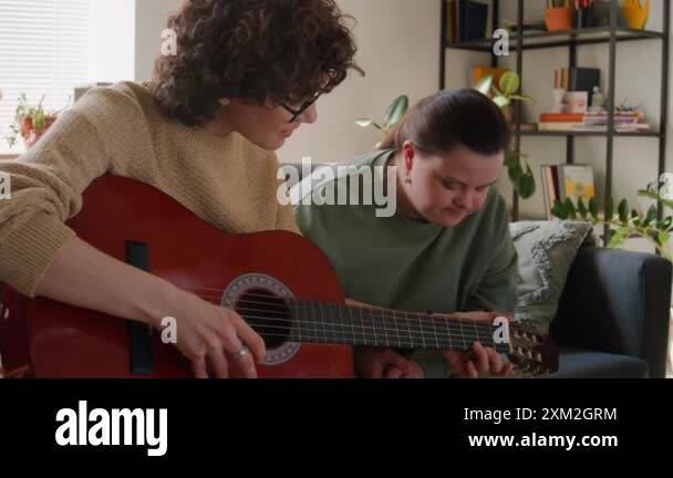 Female music tutor teaching girl with Down syndrome how to play guitar ...