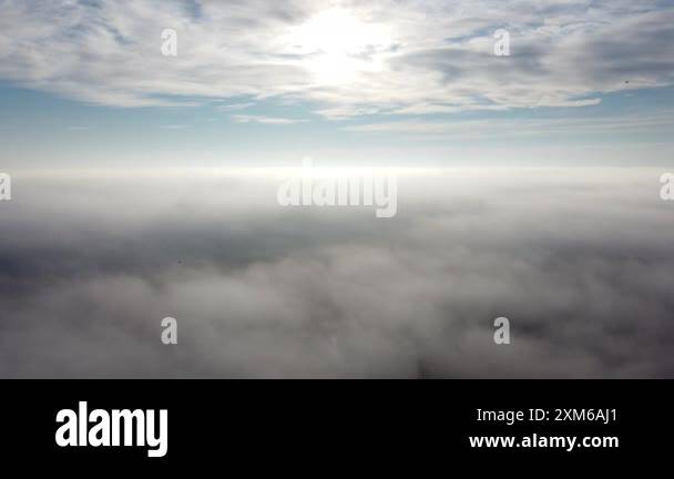 Flying over thick white fog and white clouds in blue sky with shining ...