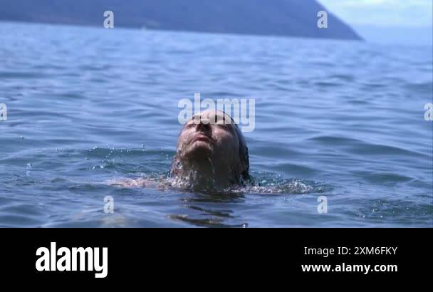 Slow-motion of a woman rising from the lake with eyes closed and a ...