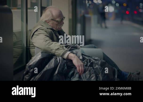 Homeless man sitting alone, bundled in plastic on train station ...