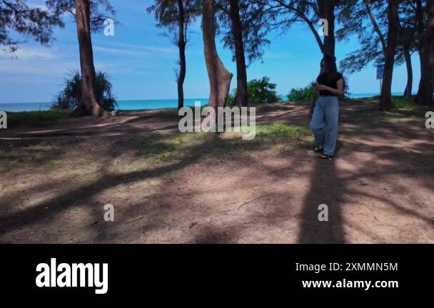 Slow motion video of a young woman walking under the shade of a pine ...