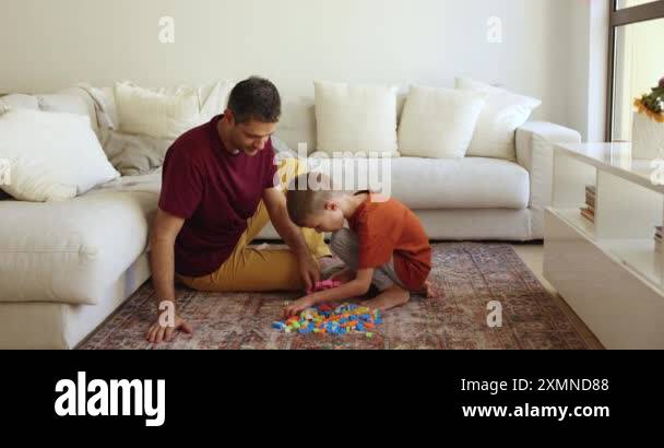 Cute little son boy and caring Latin dad playing construction game on home floor together ...