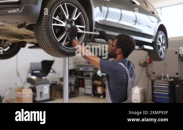 Mechanic wearing overalls working on car lifted for maintenance in ...