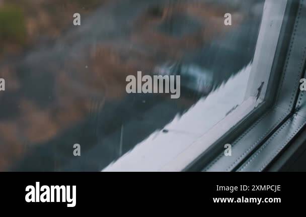 Slow motion footage of rain falling on a window, with a blurred city ...