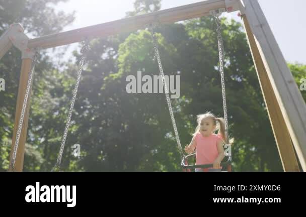 A cute little girl slides down a playground slide, her giggles echoing ...
