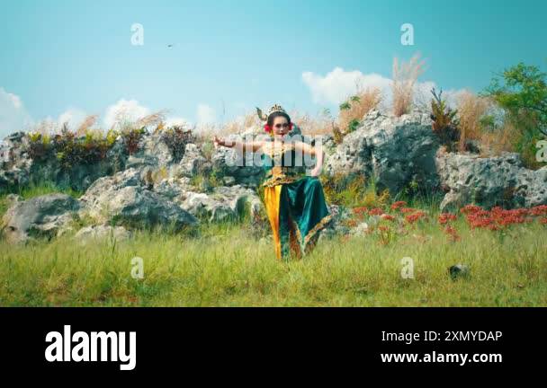 A dancer in traditional attire performs in a grassy field with rocky ...